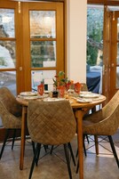 Uma área de refeições com uma mesa de madeira posta para quatro pessoas, rodeada por cadeiras acolchoadas.