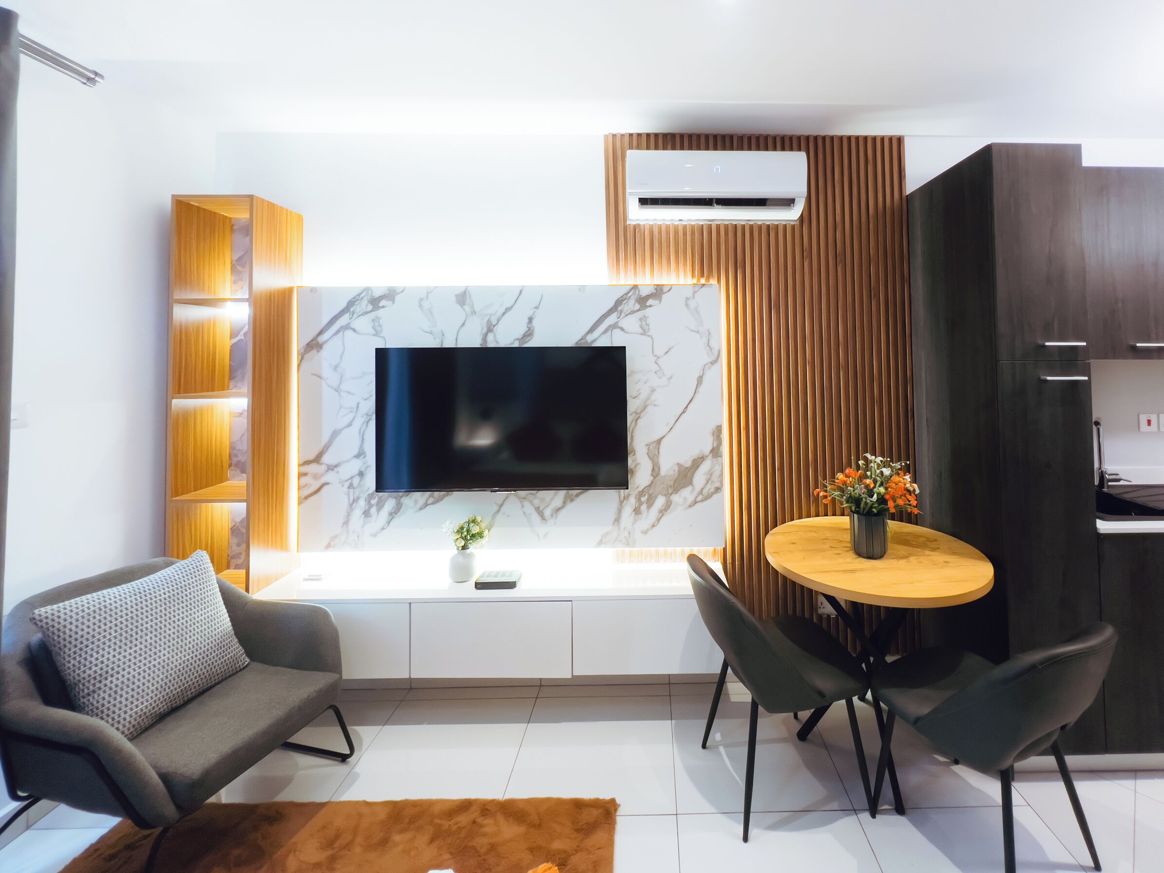 Uma sala de estar moderna com televisão de tela plana fixada em uma parede de mármore, aparador de madeira, mesa redonda de madeira com cadeiras e um sofá com almofada estampada.