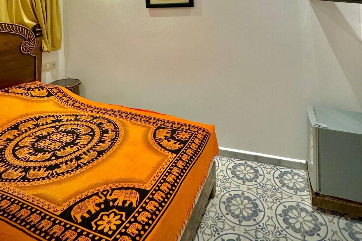 Quarto com cama, quadro na parede, tapete estampado e luminária no teto.