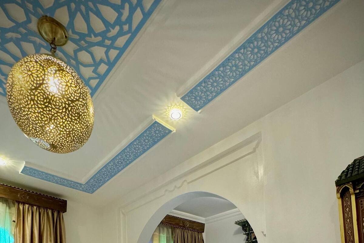 Quarto com cama grande, luminária pendente, espelho e janela com cortinas.