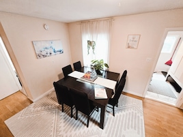 Uma área de jantar com mesa, cadeiras, uma planta e um quadro na parede.
