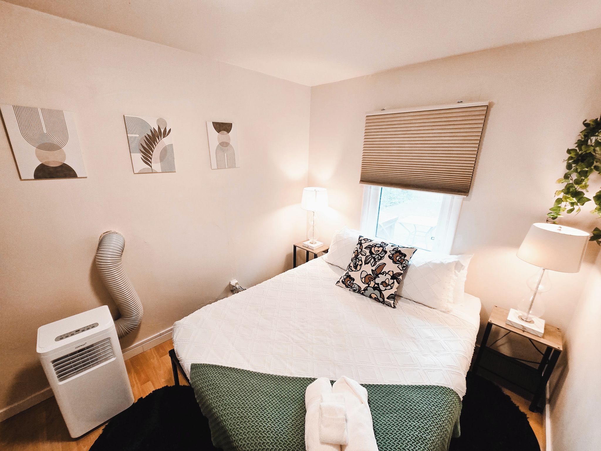 Quarto de hotel com cama, mesa de cabeceira, cadeira, janela com persianas e decoração na parede.
