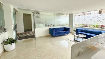 Um hall moderno com um sofá azul, uma mesa de centro de vidro e um vaso de planta.