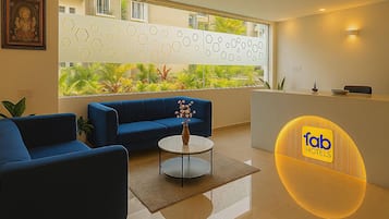 Uma área de recepção de hotel com um sofá azul, uma mesa redonda com um vaso e um balcão de recepção com um logotipo.