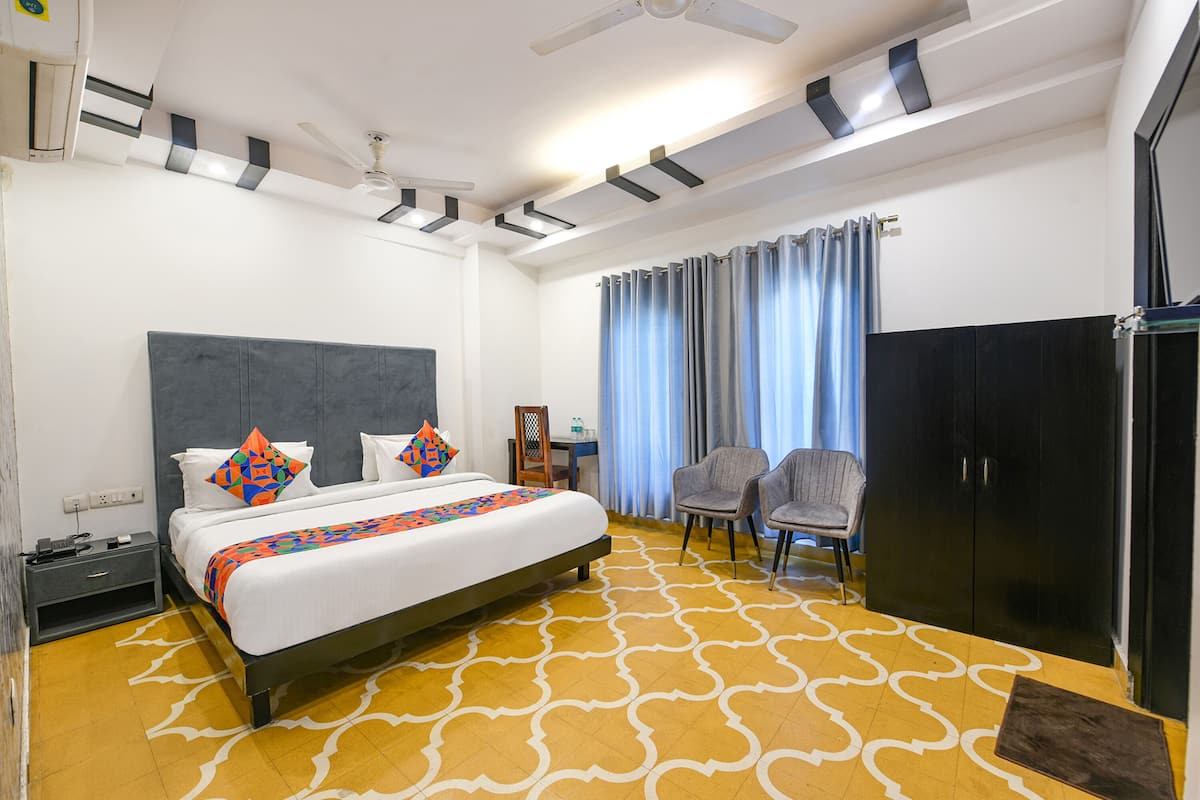 Quarto de hotel com cama, escrivaninha, cadeira, guarda-roupa e ventoinha no teto.