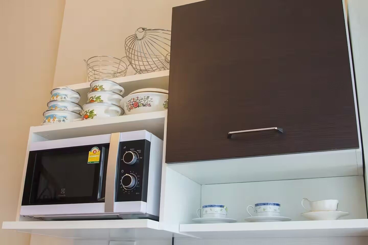 Cozinha com micro-ondas, armário e prateleira com louças.