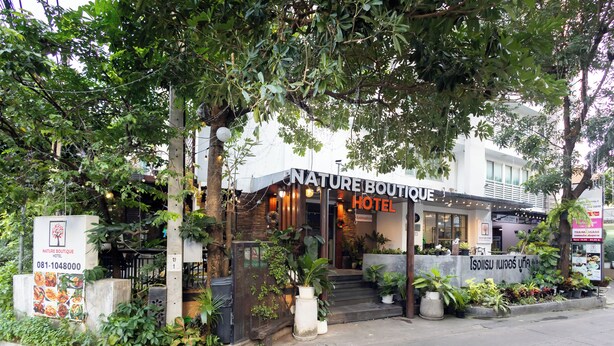 Um hotel chamado Nature Boutique Hotel, com fachada moderna, plantas externas e uma placa com informações de contato.