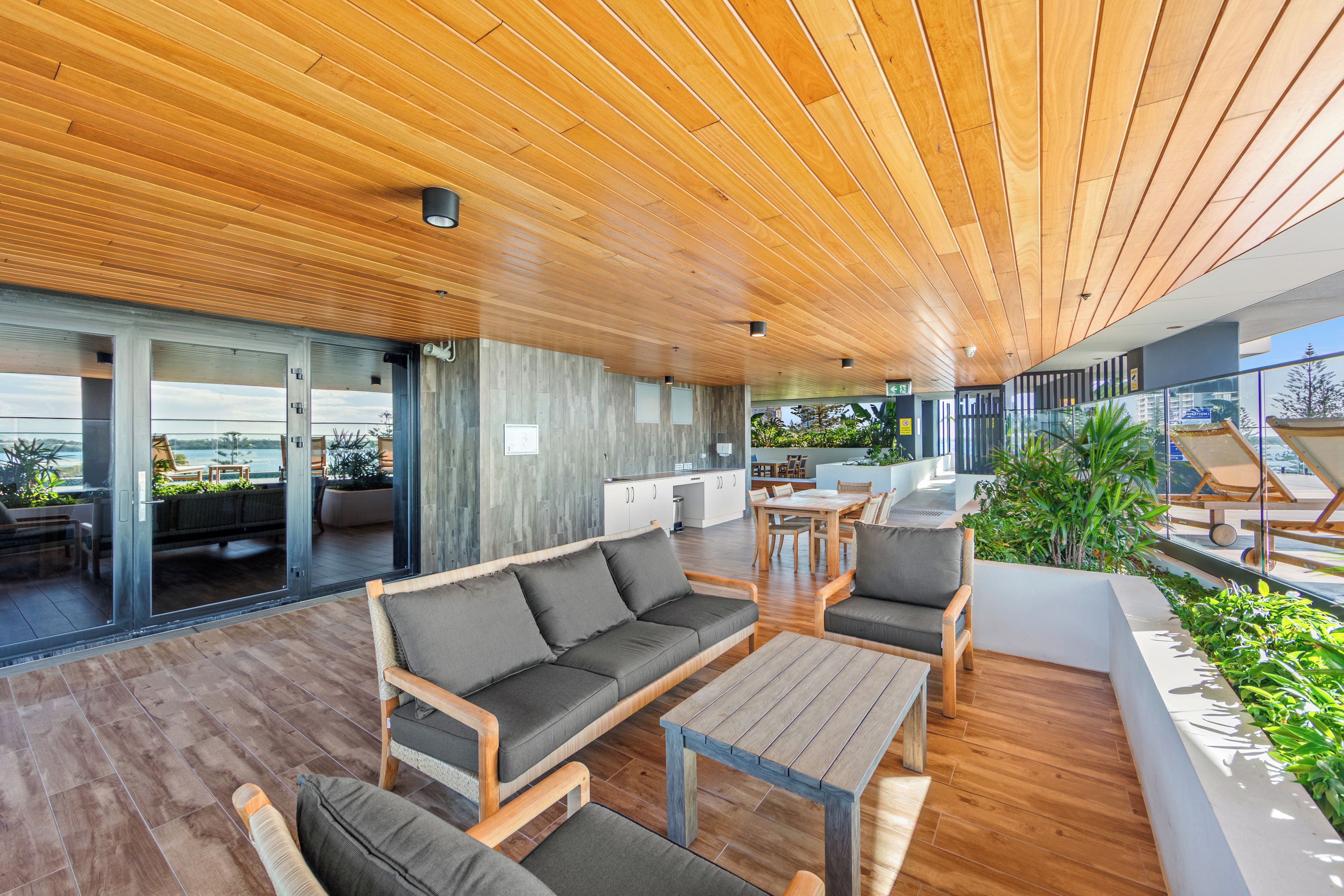 Uma área de estar moderna ao ar livre, com piso de madeira, um conjunto de sofás e uma mesa de jantar.