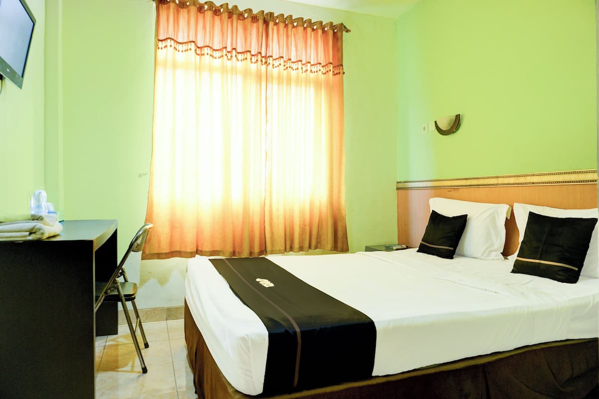 Quarto de hotel com cama, escrivaninha, cadeira e janela com cortinas.