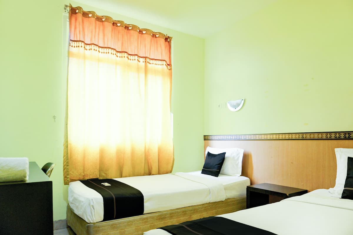 Quarto de hotel com duas camas de solteiro, mesa de cabeceira, escrivaninha e janela com cortinas.