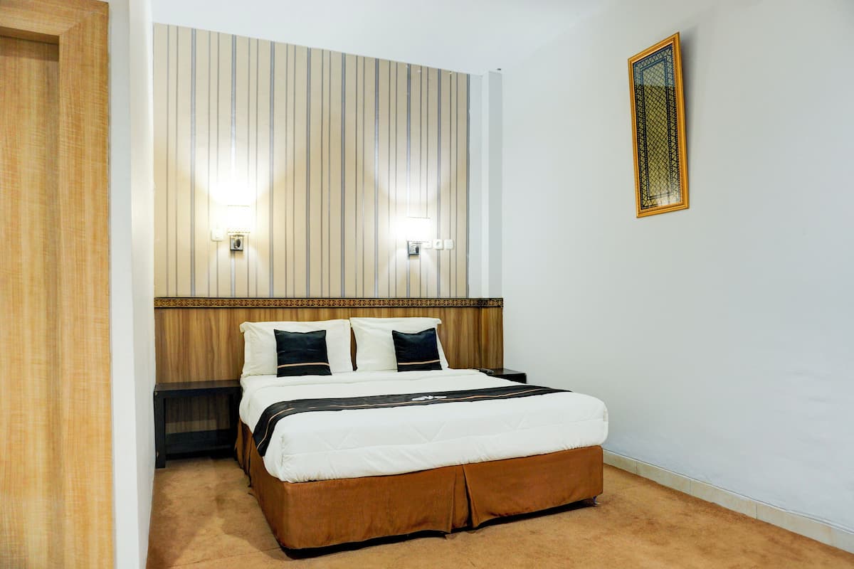 Quarto de hotel bem arrumado com uma cama grande, cabeceira de madeira e duas luminárias fixadas na parede.