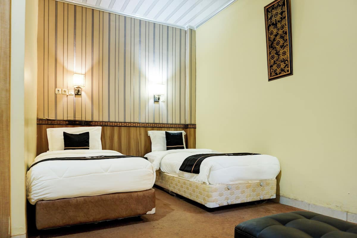 Quarto de hotel com duas camas, cabeceira de madeira, luminária fixada na parede e um ornamento decorativo na parede.