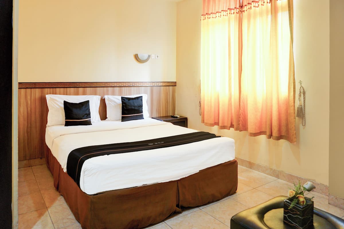 Quarto de hotel com uma cama grande, mesa de cabeceira, luminária e uma pequena mesa com um vaso.