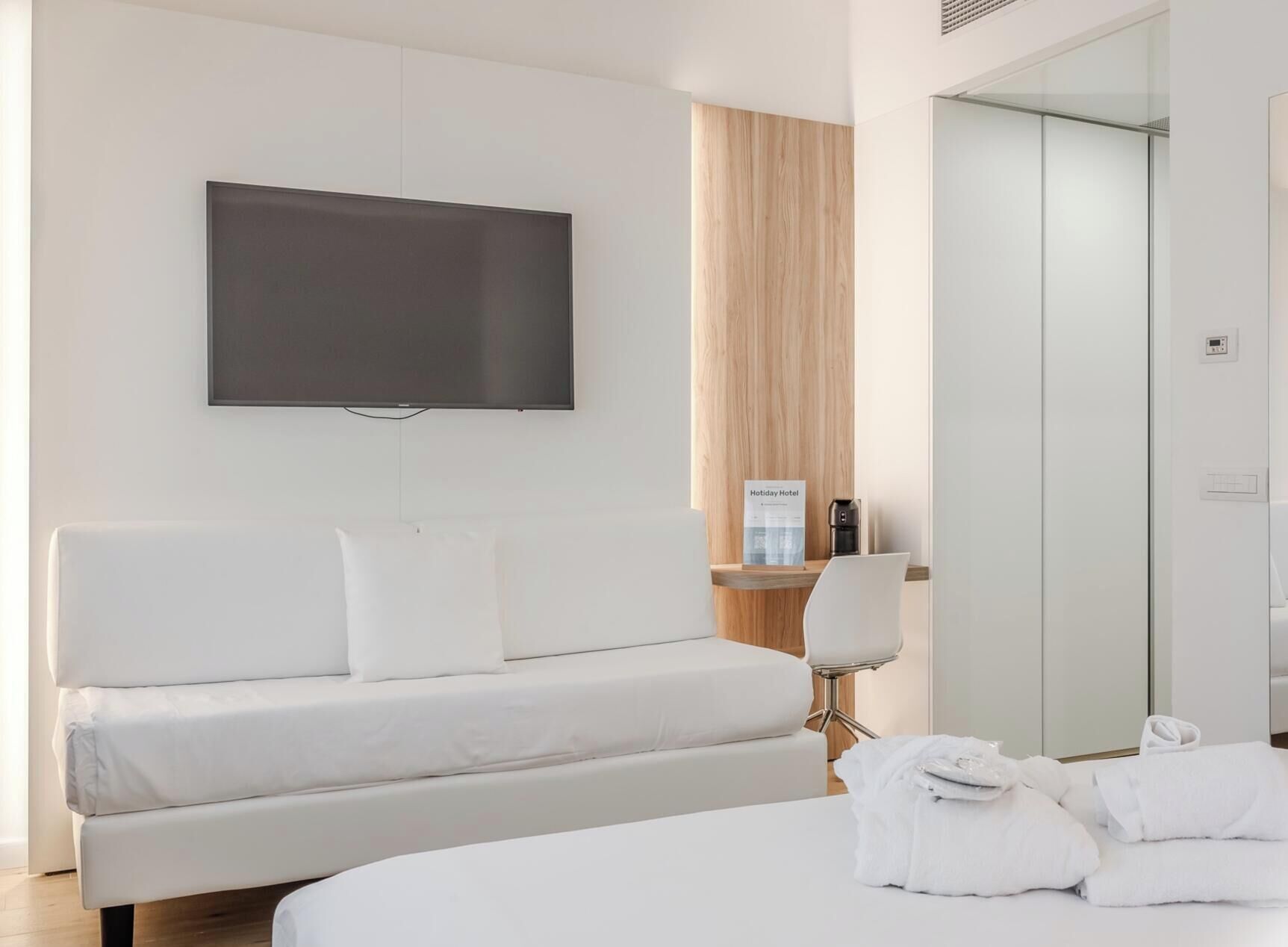 Quarto de hotel moderno com uma cama grande, TV de tela plana na parede, parede de destaque em madeira, uma mesinha com cafeteira e um espelho.