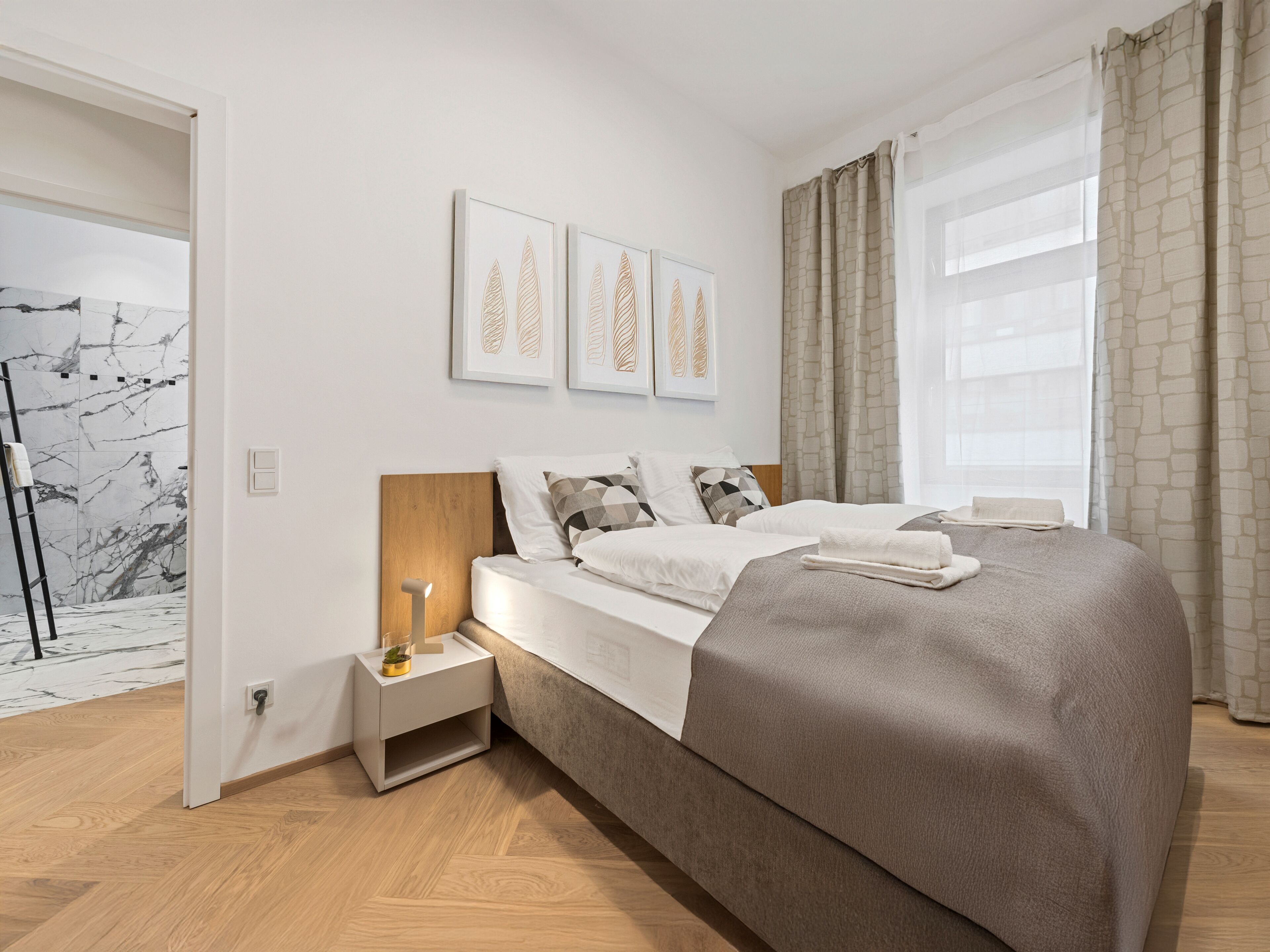 Quarto moderno com uma cama grande, mesa de cabeceira com abajur e obras de arte na parede.
