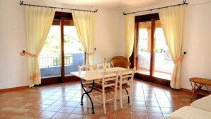 Quarto com mesa de jantar e cadeiras, um banco e vista para uma varanda.