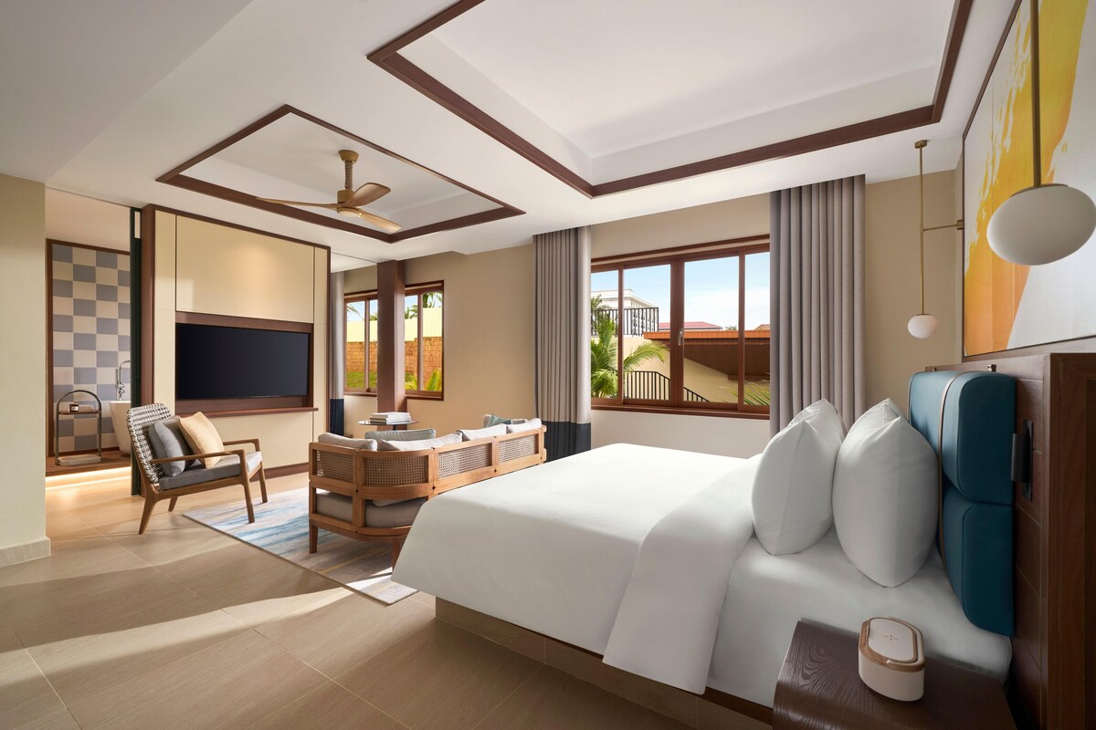 Quarto de hotel com uma cama grande, escrivaninha, cadeira, televisão e vista para o exterior.