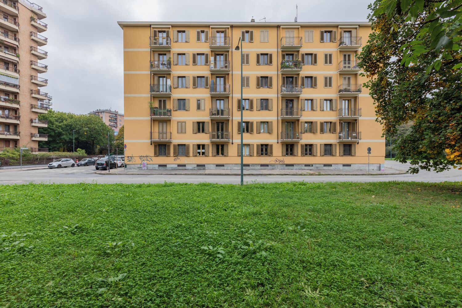 Um edifício residencial com vários andares, varandas, área de estacionamento e um gramado à frente.