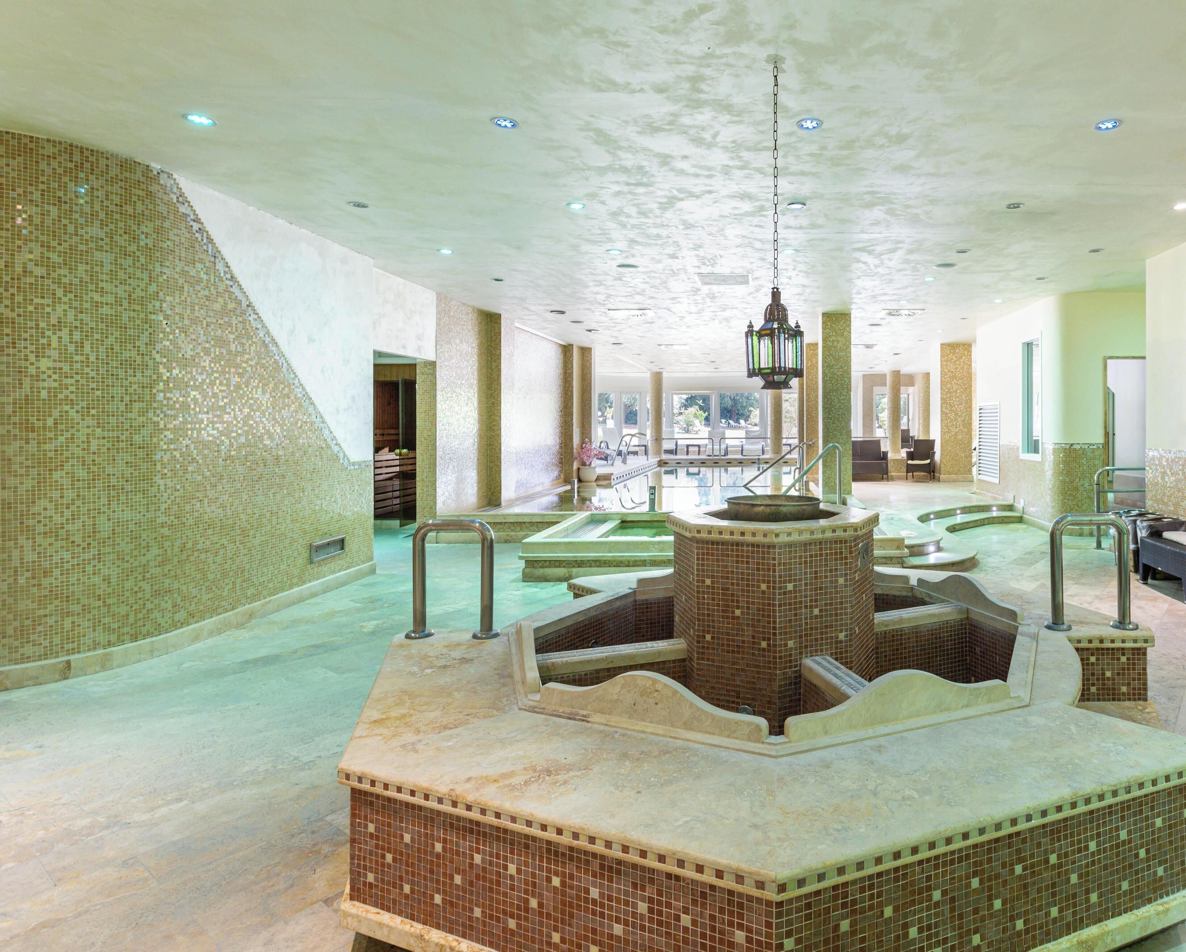 Uma área de spa com uma banheira de hidromassagem central, áreas de estar e vista para o exterior.