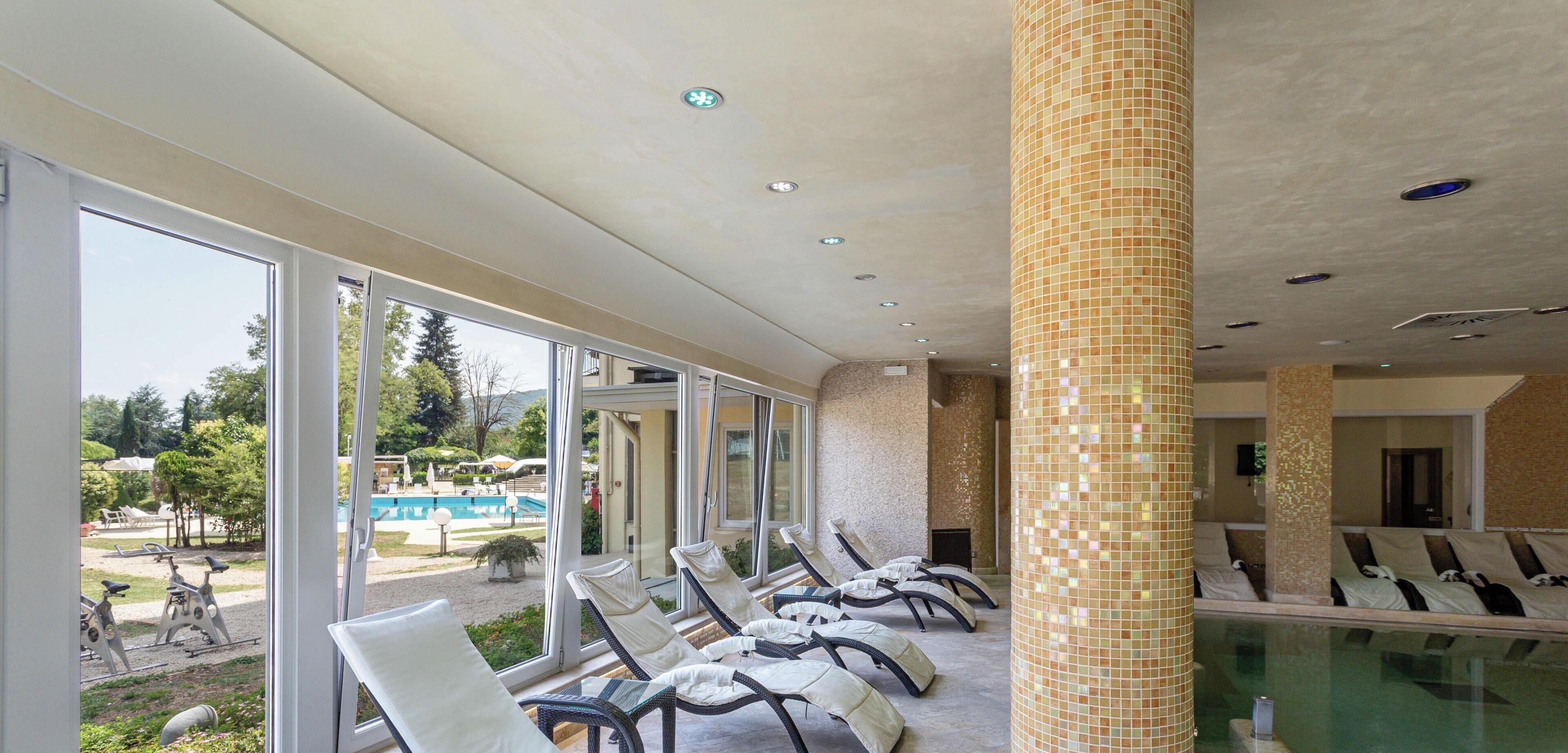 Área interna com piscina iluminada pelo sol, cadeiras de descanso e vista para o exterior.