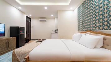 Quarto de hotel com uma cama grande, televisão, frigorífico e parede estampada.