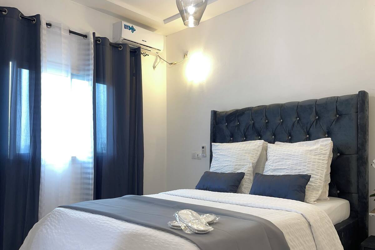 Quarto de hotel com uma cama grande, cortinas escuras, aparelho de ar condicionado e uma mesa de cabeceira.