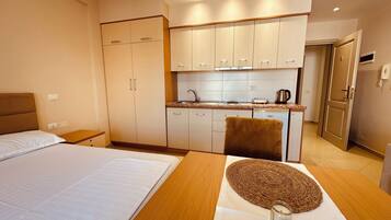 Quarto de hotel pequeno com cama, mesa de jantar com jogos americanos, área de cozinha com armários e porta de banheiro.