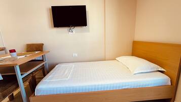 Quarto com cama de madeira, televisão de tela plana na parede, escrivaninha com cadeira e uma mesinha com uma xícara vermelha.