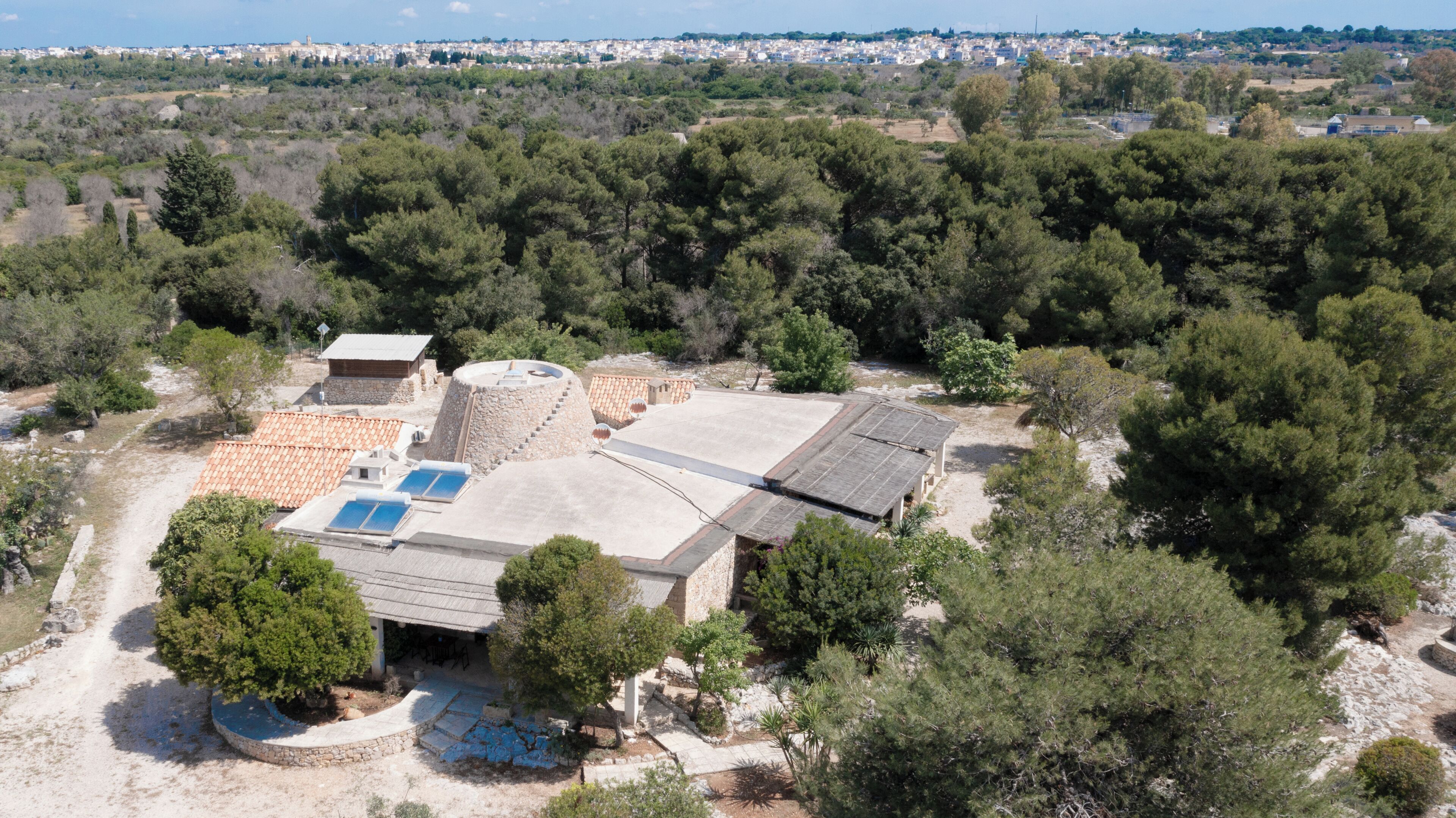 Uma villa com um pátio de pedra, painéis solares e vista para uma cidade costeira.