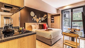 Quarto de hotel moderno com cozinha, uma cama com encosto, mesa de jantar com cadeiras e uma grande janela com vista.
