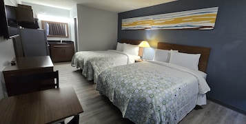 Quarto de hotel com duas camas, uma escrivaninha e uma cadeira. Há um quadro na parede e um abajur na mesa de cabeceira.
