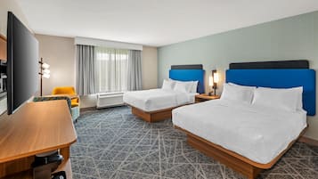 Quarto de hotel com duas camas, uma escrivaninha, uma cadeira e uma televisão.