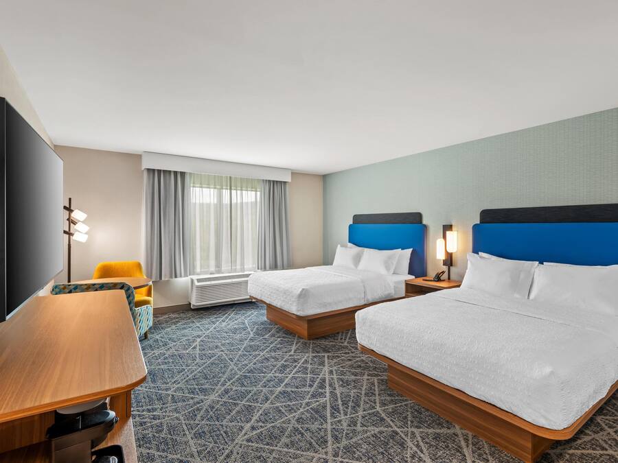 Quarto de hotel com duas camas, uma escrivaninha, uma cadeira e uma televisão.