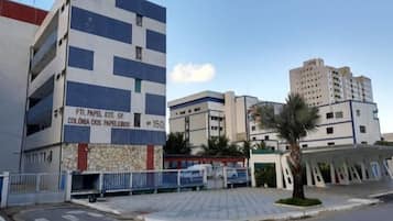 Um edifício de vários andares com fachada em azulejos, uma placa indicando 'FTI. PAPEL. EST. SP. COLONIA DOS PAPELEROS', e uma área de estacionamento com uma palmeira e uma cobertura.