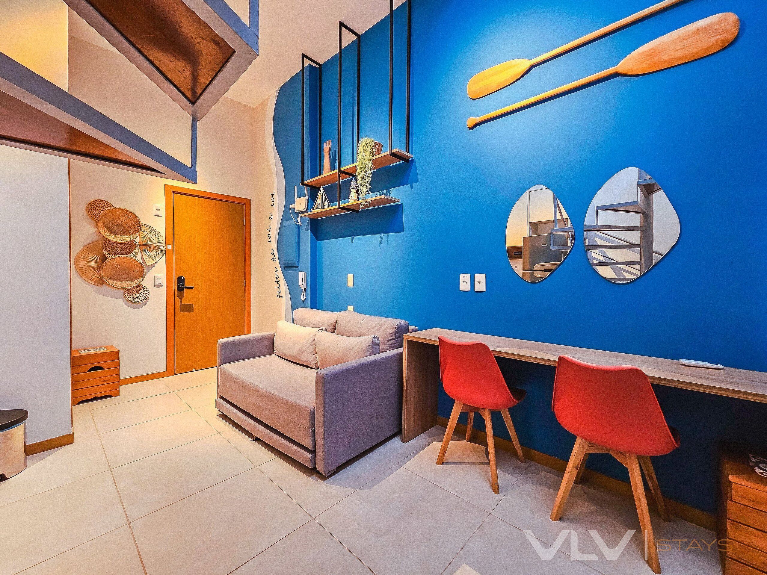 Um interior moderno com uma parede azul de destaque, um sofá, duas cadeiras vermelhas, uma escrivaninha de madeira e um espelho.