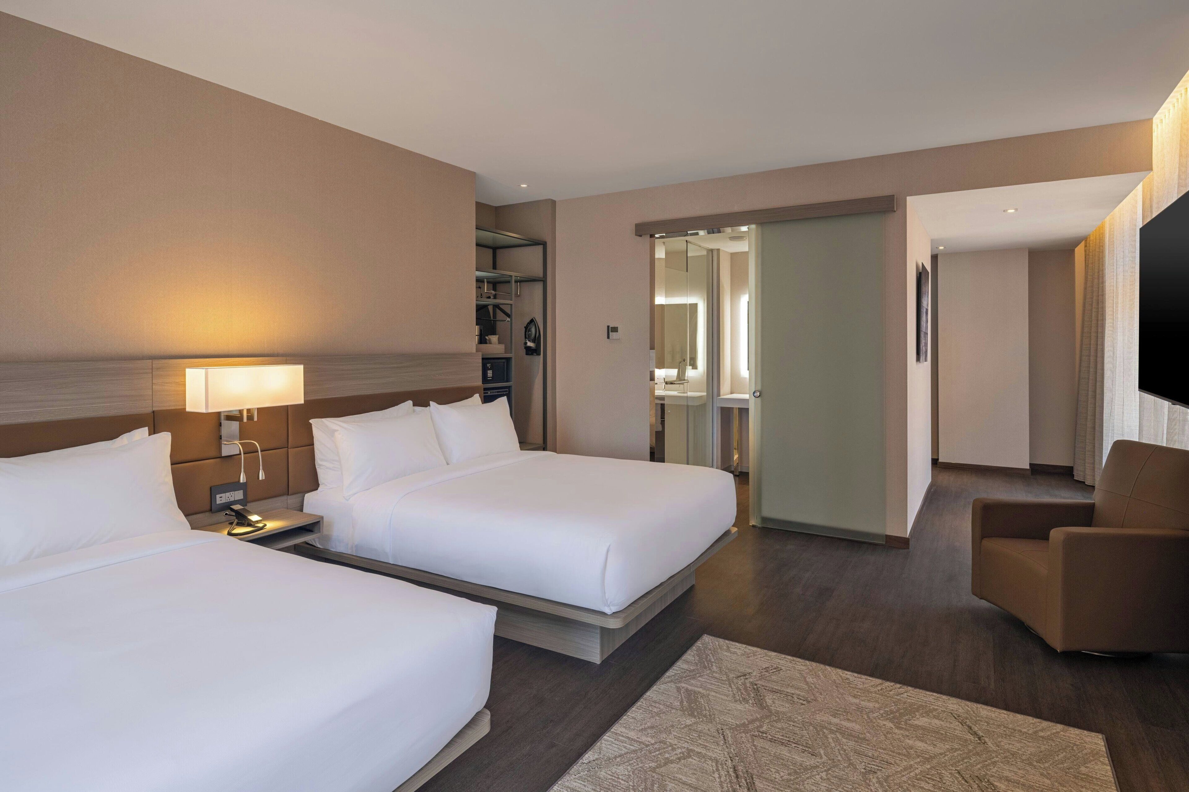 Quarto de hotel com duas camas, uma mesa, uma cadeira e uma televisão.