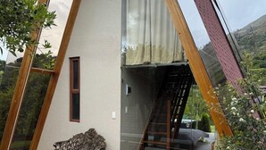 Uma casa moderna com design triangular único, porta de vidro que dá para um quarto e uma pequena área externa com um banco.
