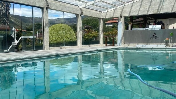 Piscina interna translúcida com teto de vidro, rodeada por paredes de pedra e vista para uma paisagem montanhosa.
