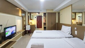 Quarto de hotel com duas camas, uma secretária com cadeira, televisão e guarda-roupa.