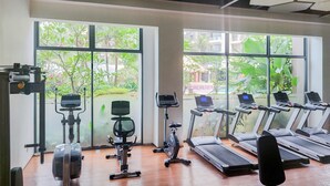 Uma academia com equipamentos de ginástica, grandes janelas e vista para o verde.