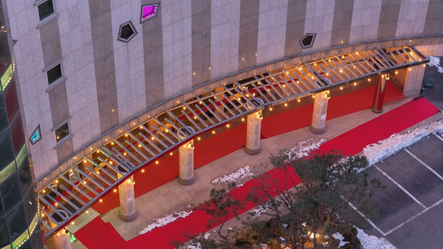 Um átrio de hotel com tapete vermelho, colunas e uma escadaria curva.