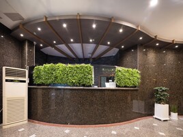 Uma área de recepção com teto curvo, unidade de ar condicionado embutida e balcão de atendimento com uma planta verde.