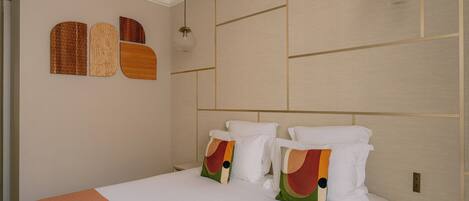 Quarto de hotel com uma cama grande, duas mesas de cabeceira, uma parede com padrões geométricos e um lustre.