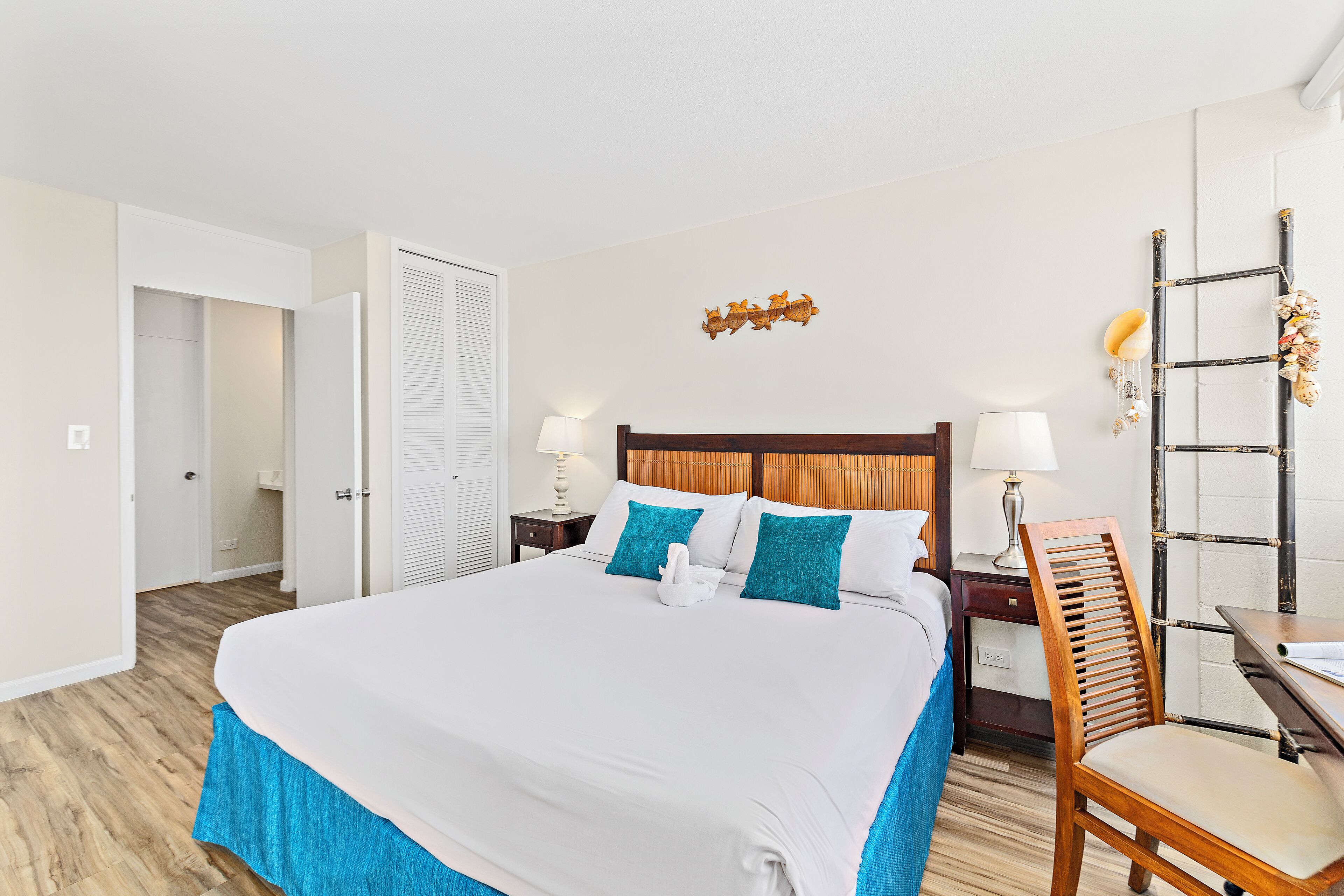 Quarto de hotel bem organizado, com uma cama grande, duas mesas de cabeceira com luminárias, uma cadeira de madeira e uma pequena escrivaninha.