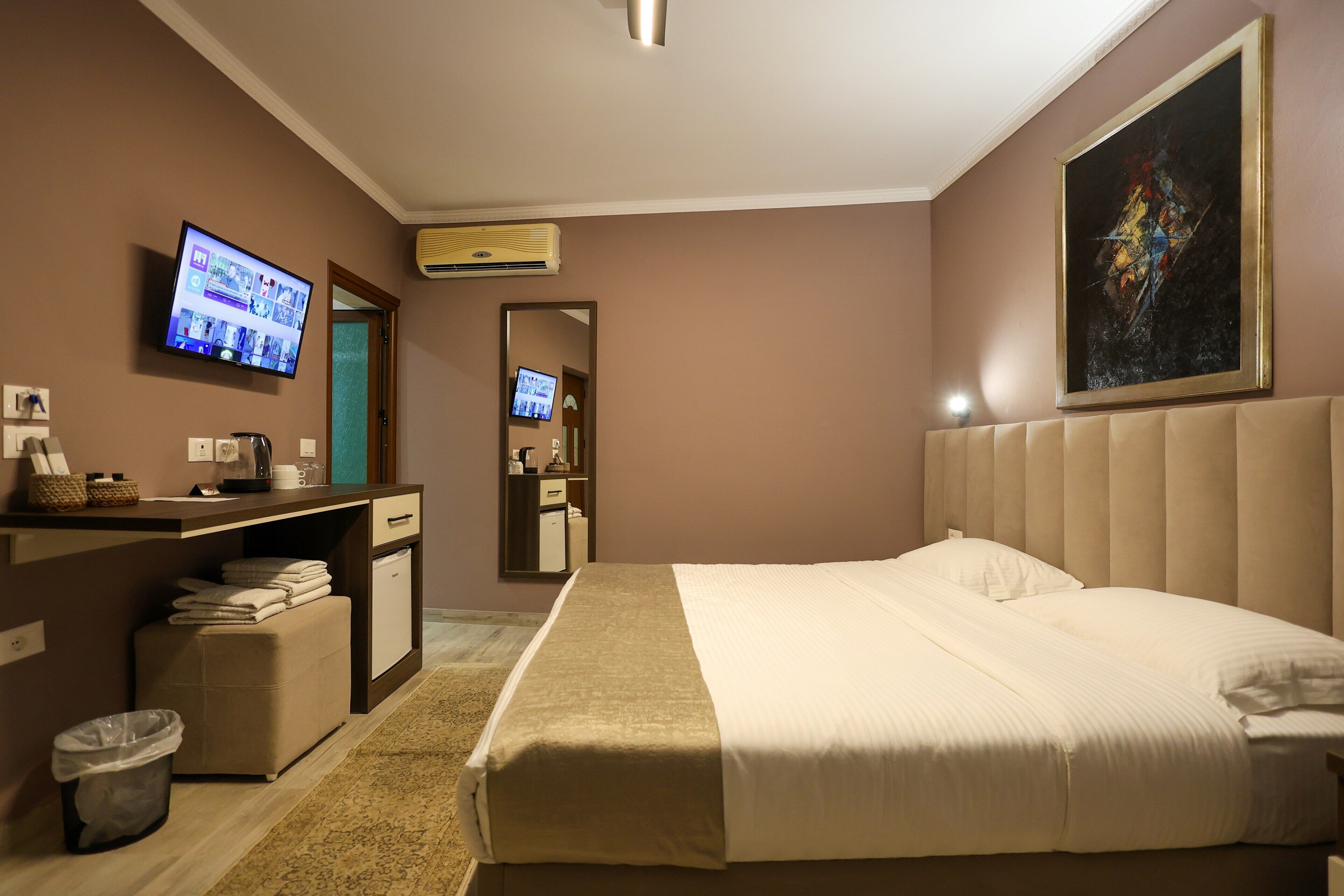 Quarto de hotel com cama, escrivaninha, televisão e um quadro na parede.