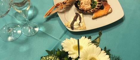 Uma mesa posta com uma travessa de frutos do mar, taças de vinho e um arranjo floral.