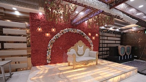 Um palco com sofá branco, painel de madeira e um fundo floral vermelho.