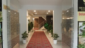 Entrada de hotel com tapete vermelho, plantas em vasos e escadaria que dá acesso aos quartos.