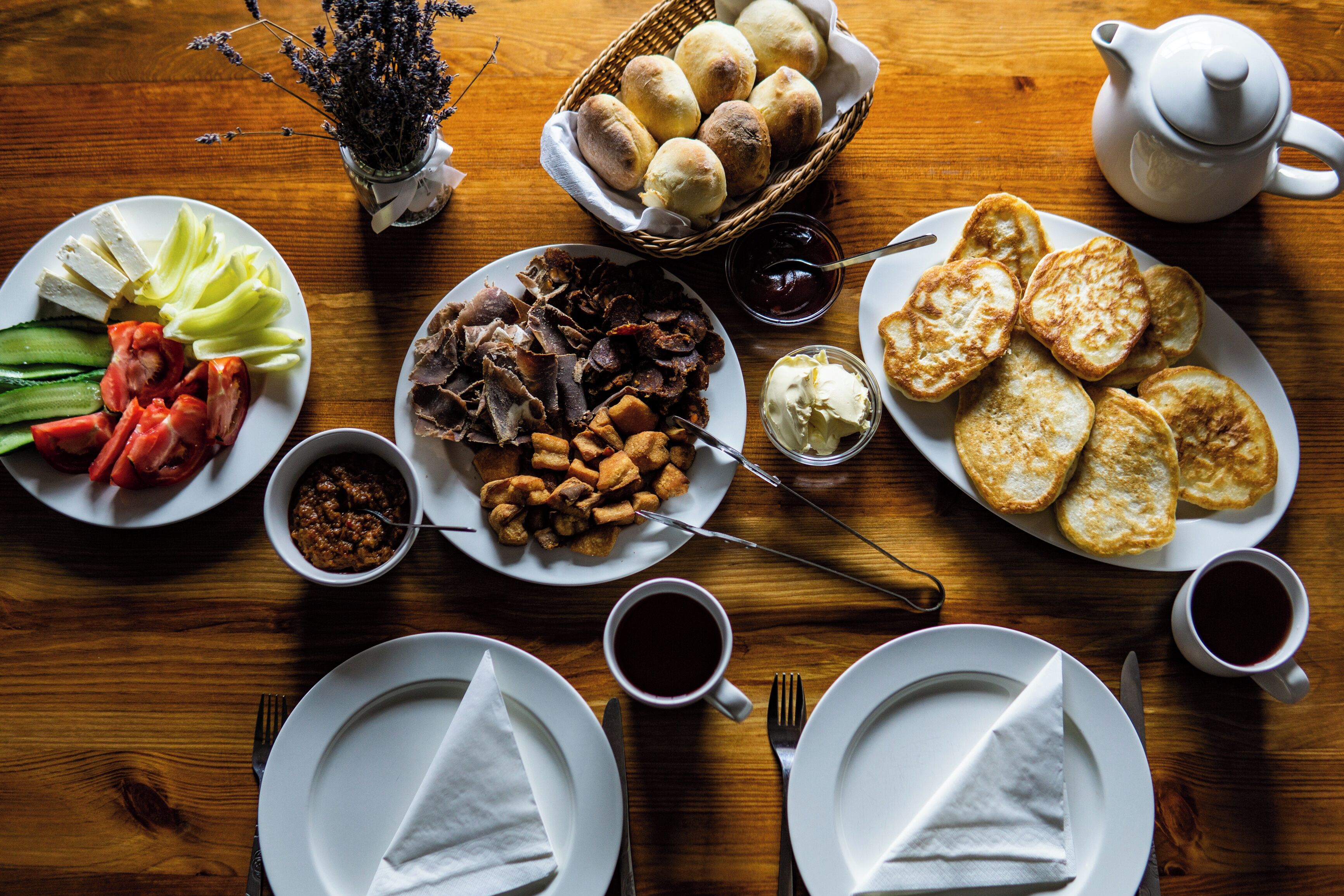 Uma mesa de madeira com diversos alimentos, pratos e uma chaleira.