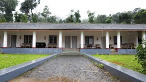 Um edifício em estilo colonial com fachada simétrica, várias portas e varanda coberta com assentos.